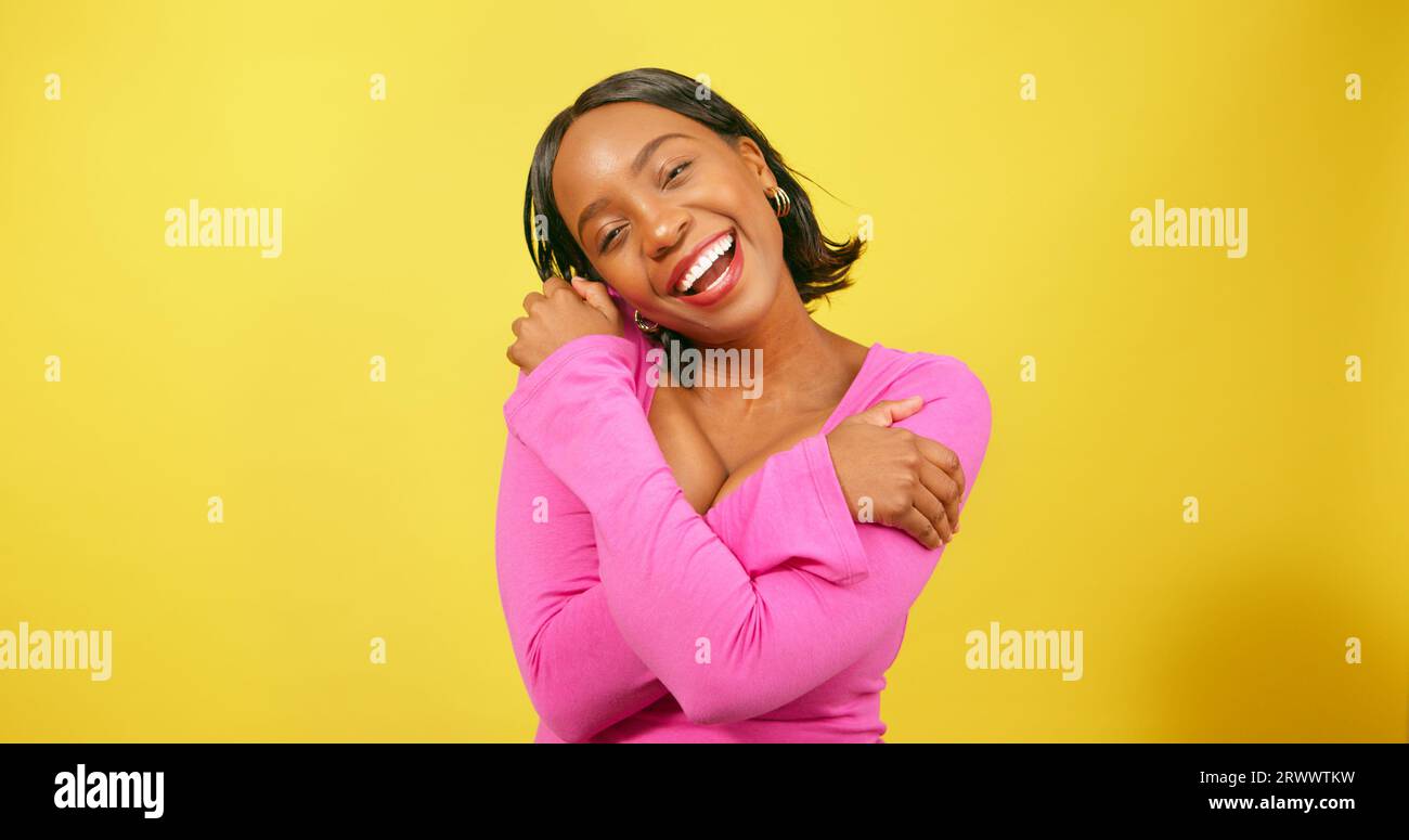 Black woman rubs arms, hugging, self love concept, yellow studio ...