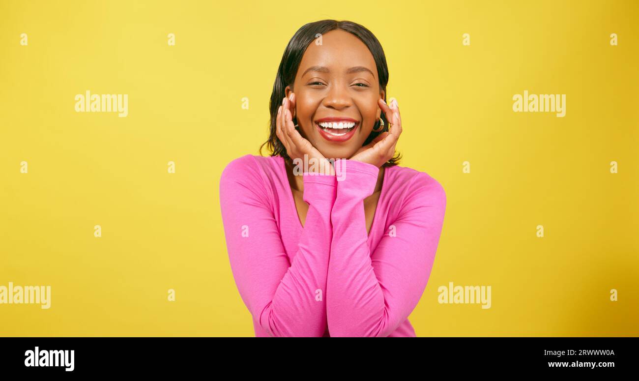 Beautiful Black woman cups hands under chin in cute pose, yellow studio ...