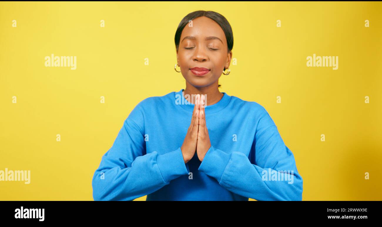 Calm young woman puts hands into prayer position, praying, yellow ...