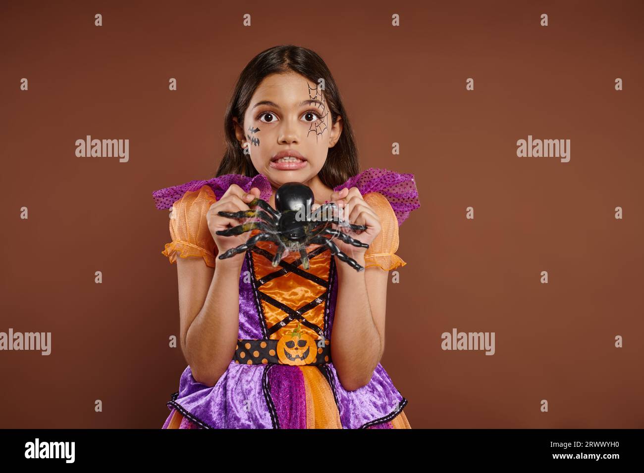 spooky girl in Halloween costume holding fake spider and grimacing on ...