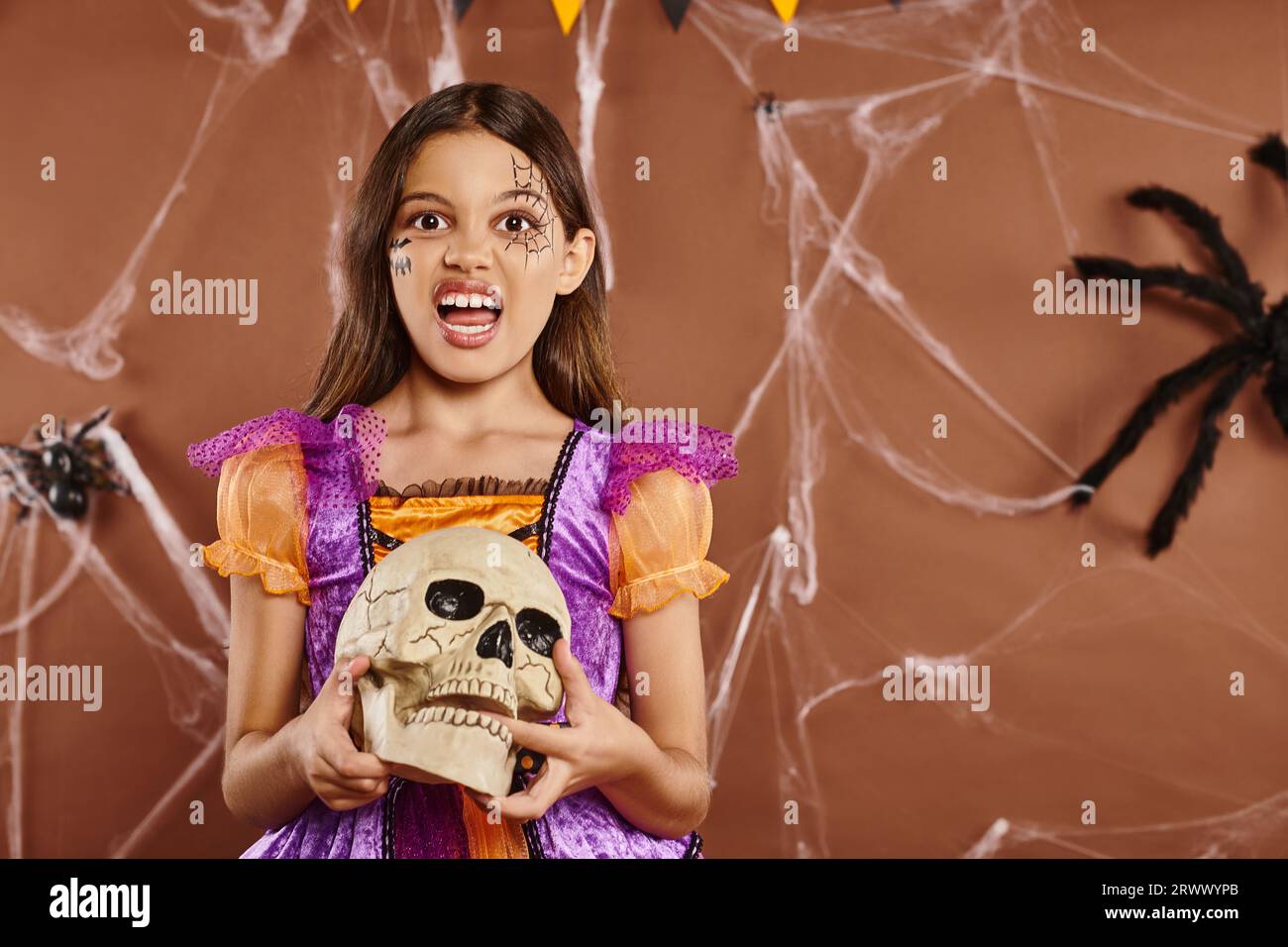 girl in Halloween costume holding skull and growling at camera on brown ...