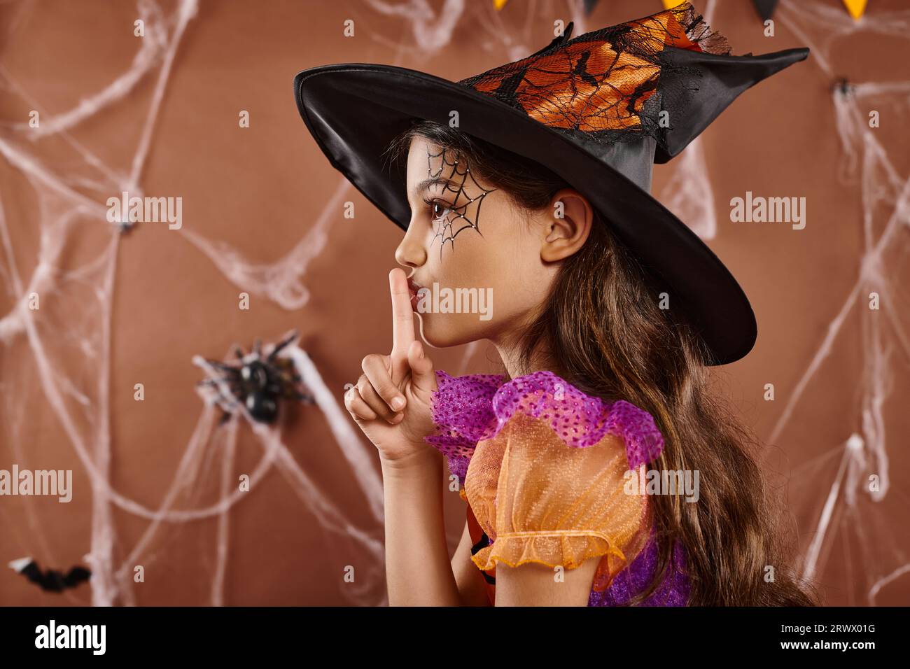 cute little girl in Halloween witch costume and pointed hat showing shh ...