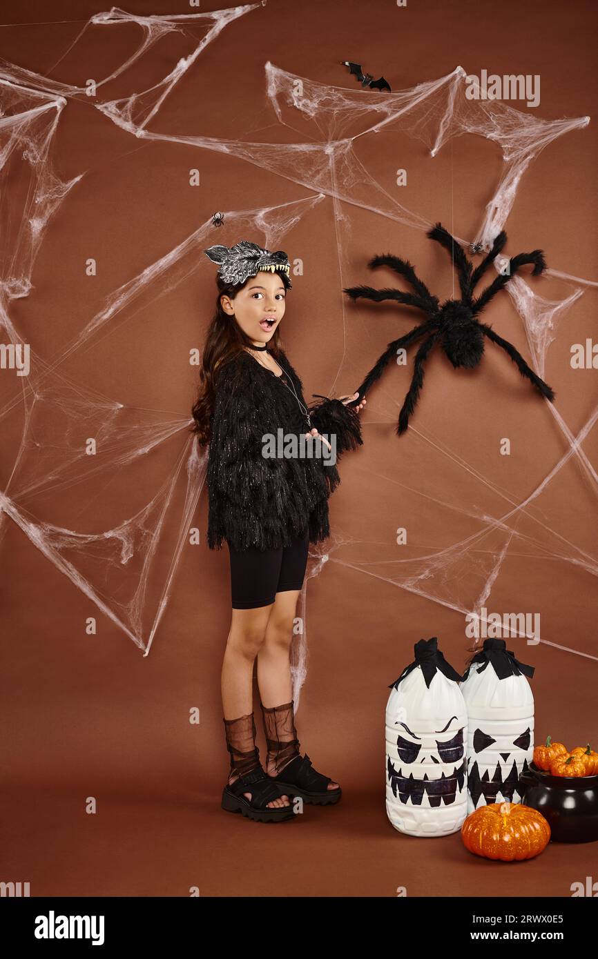 surprised preteen girl in black outfit touching spider on brown ...