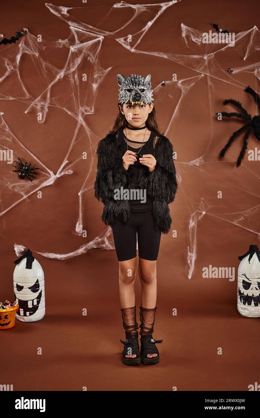 cute girl in faux fur attire with wolf mask standing still on brown ...