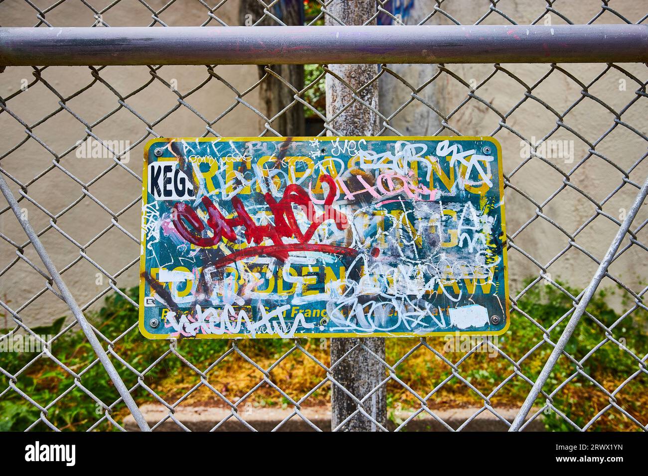 Graffiti on sign with messages on chain link fence for Trespassing ...
