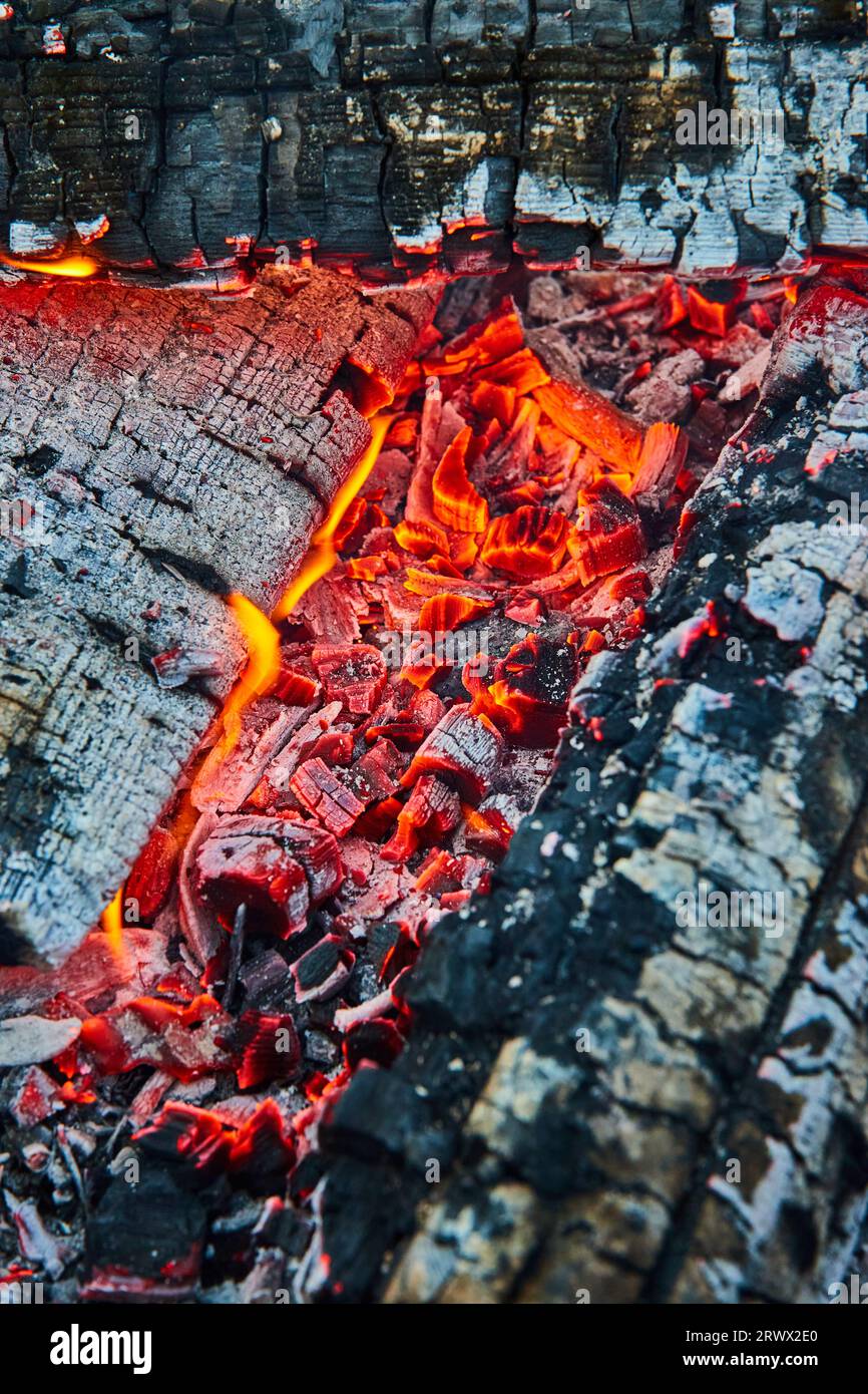 Close up of glowing red embers wedged between three blackened logs and ...