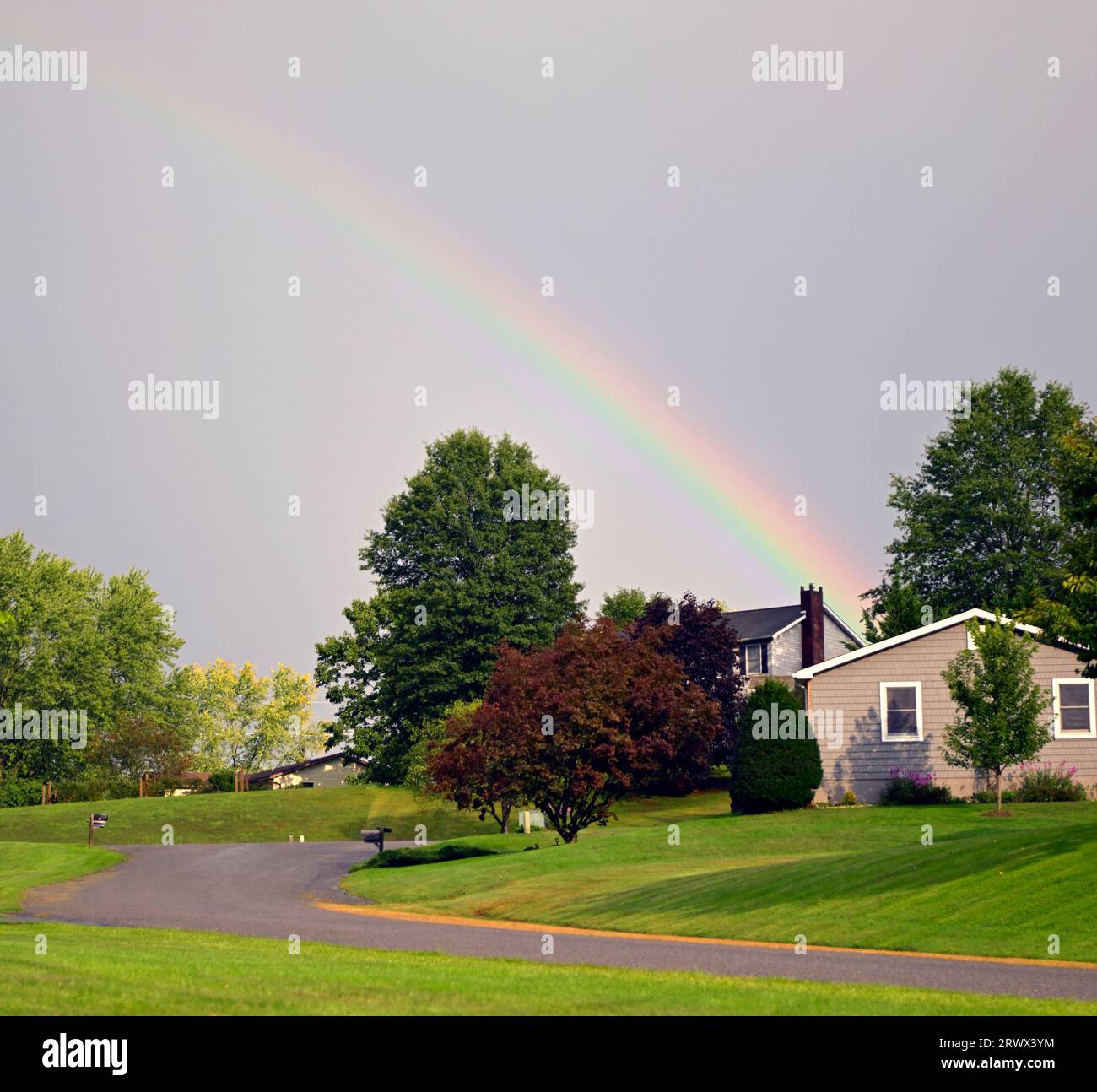 A vibrant rainbow arching over a suburban neighborhood, encasing the ...