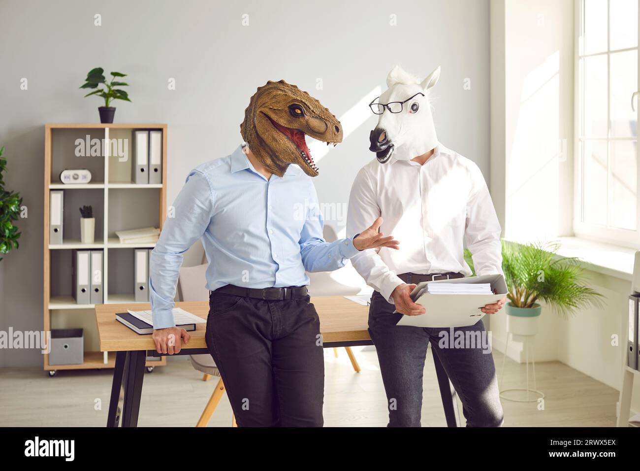 Two young workers in funny lizard and horse masks standing by office ...