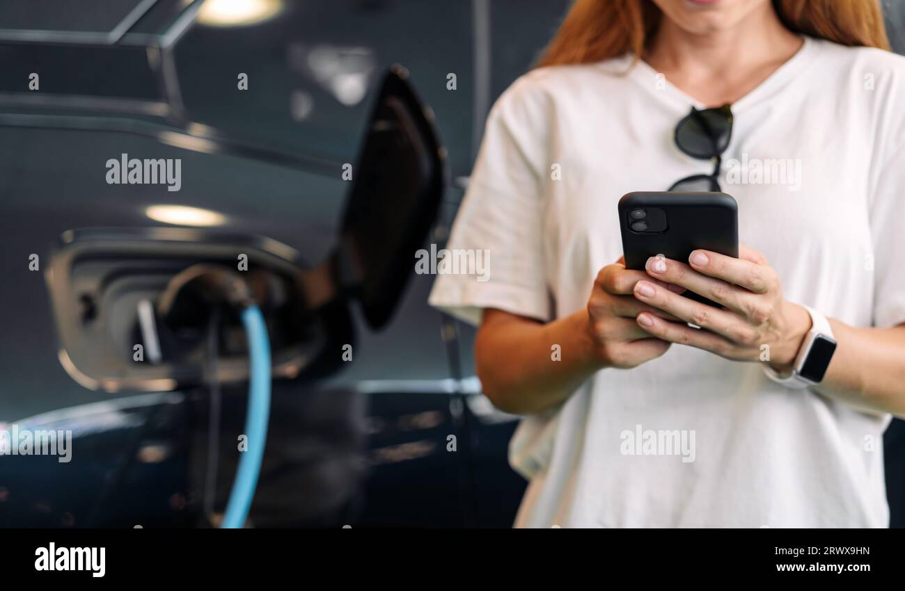 Female person using her mobile phone for charging her electric car. EV ...