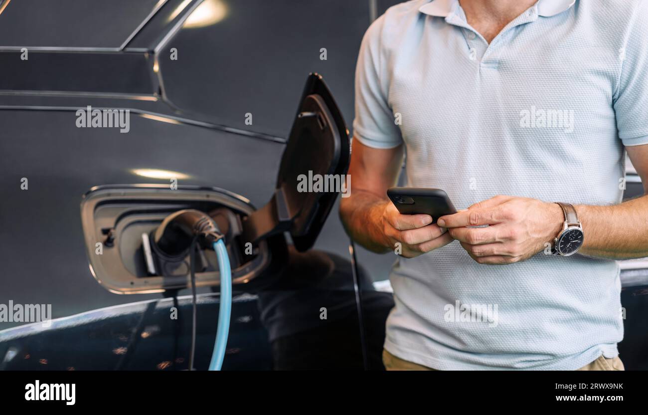 Male person using his smart phone for charging electric car. EV and ...