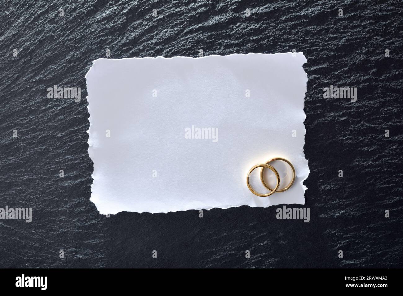White textured paper card with two engagement rings on slate base table ...