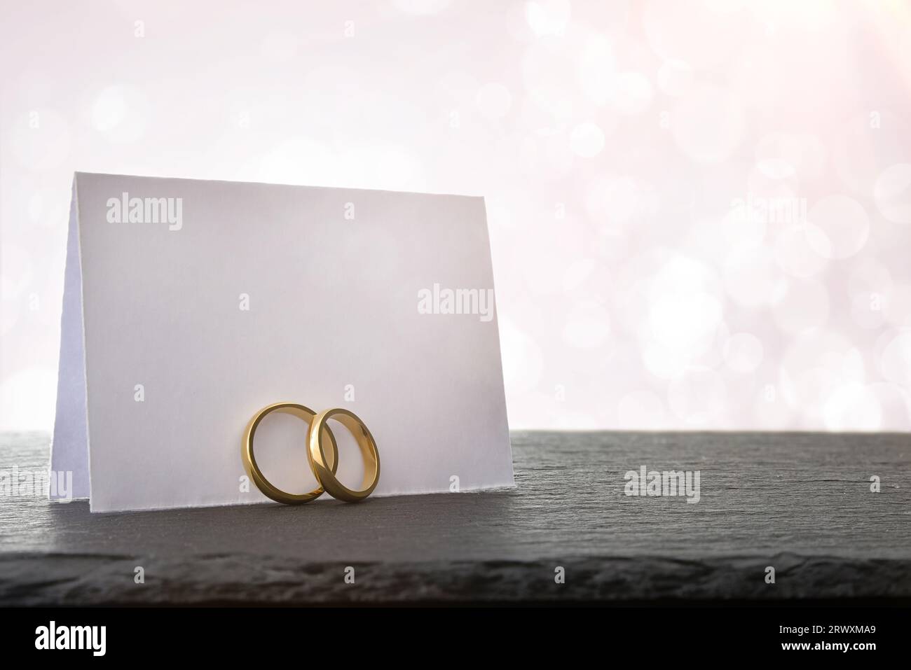 Two engagement rings on slate table with blank paper sign behind with ...