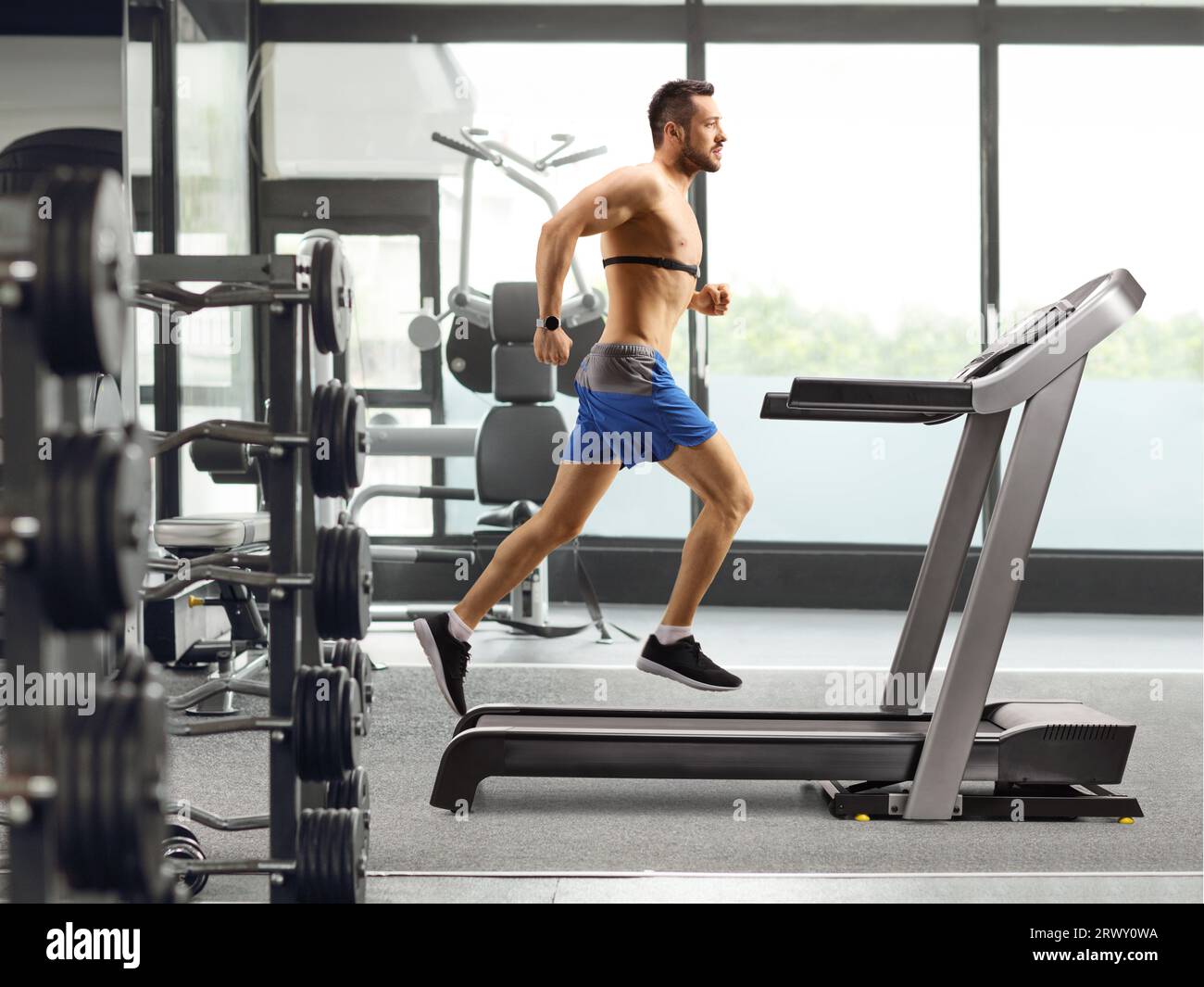 Full length profile shot of a young man running on a treadmill and ...
