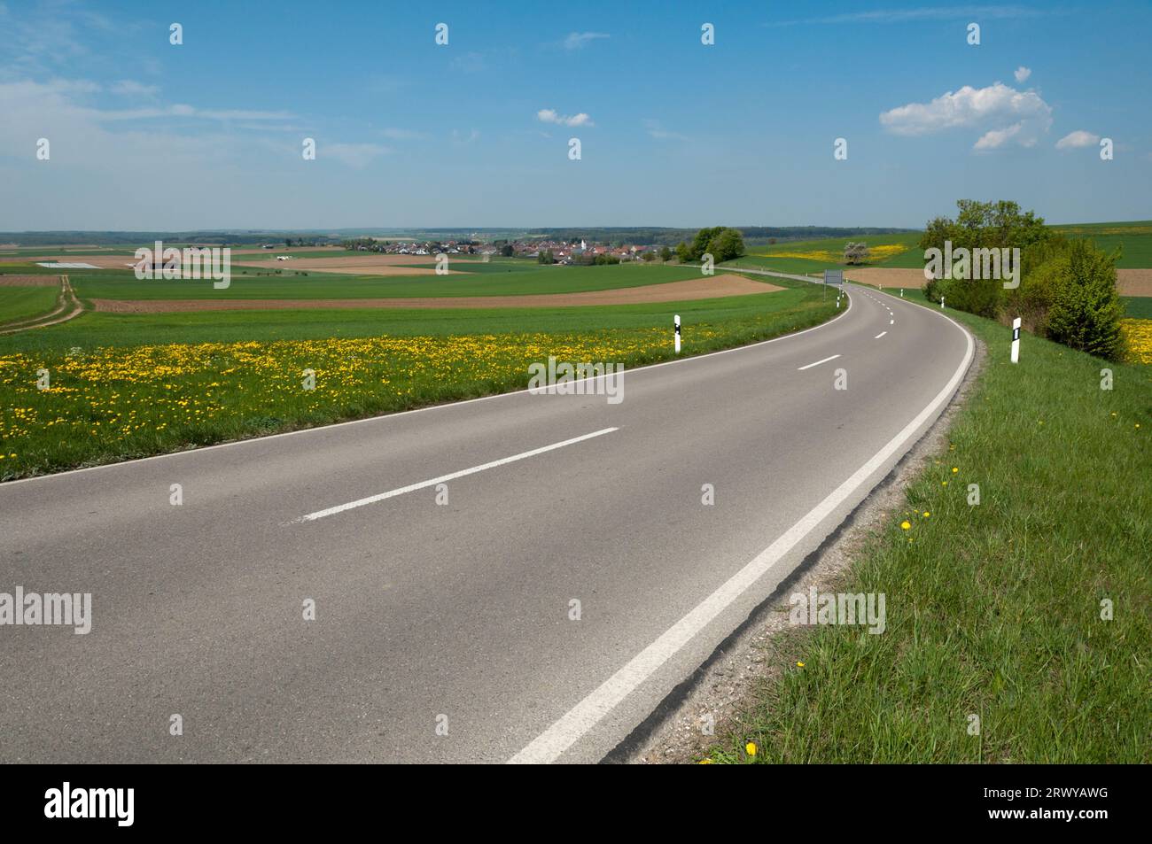 Rural two-lane roadway passing through lush farmlands with white ...