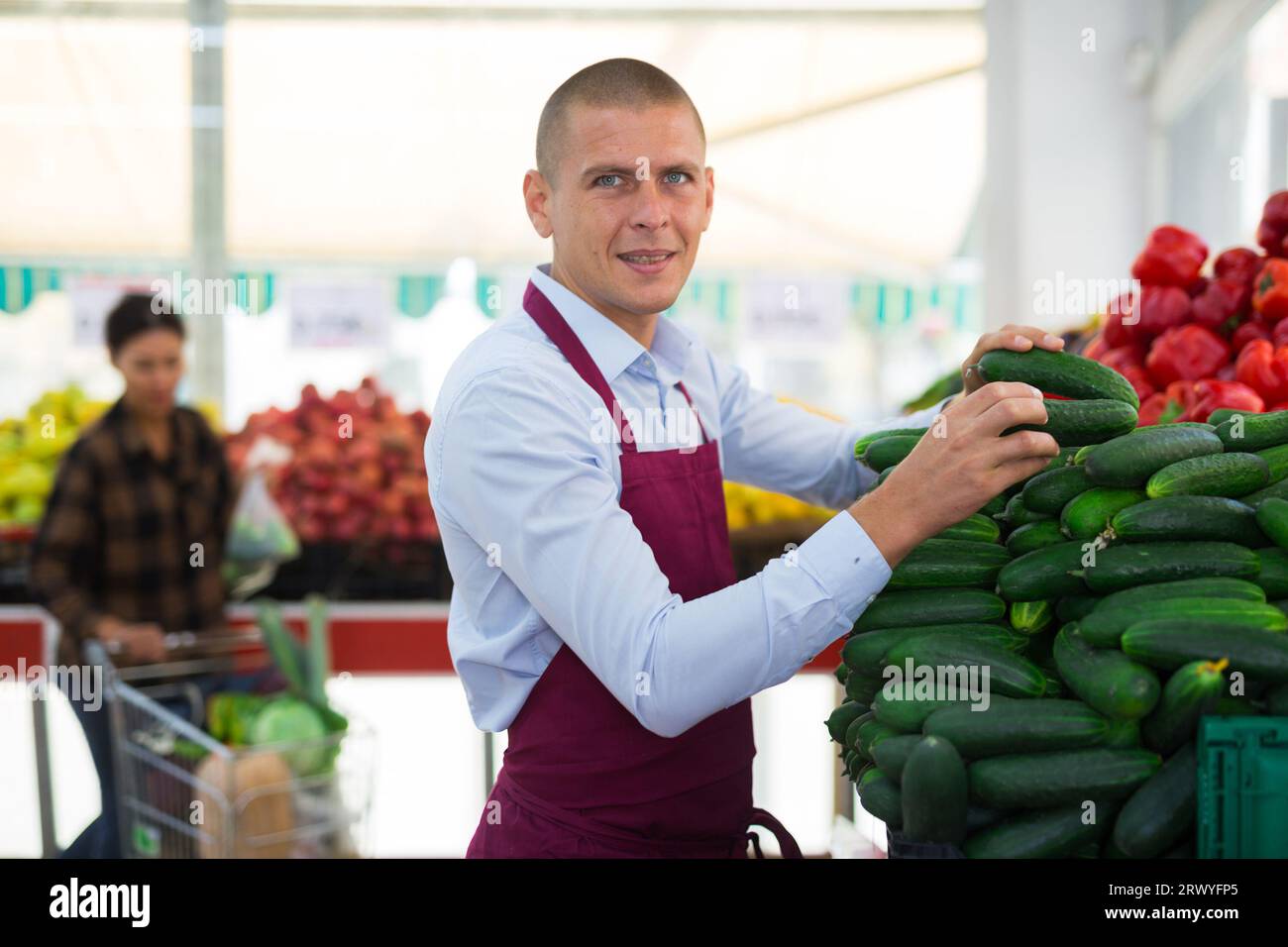 Smiling greengrocery owner laying out fruits and vegetables on counter ...