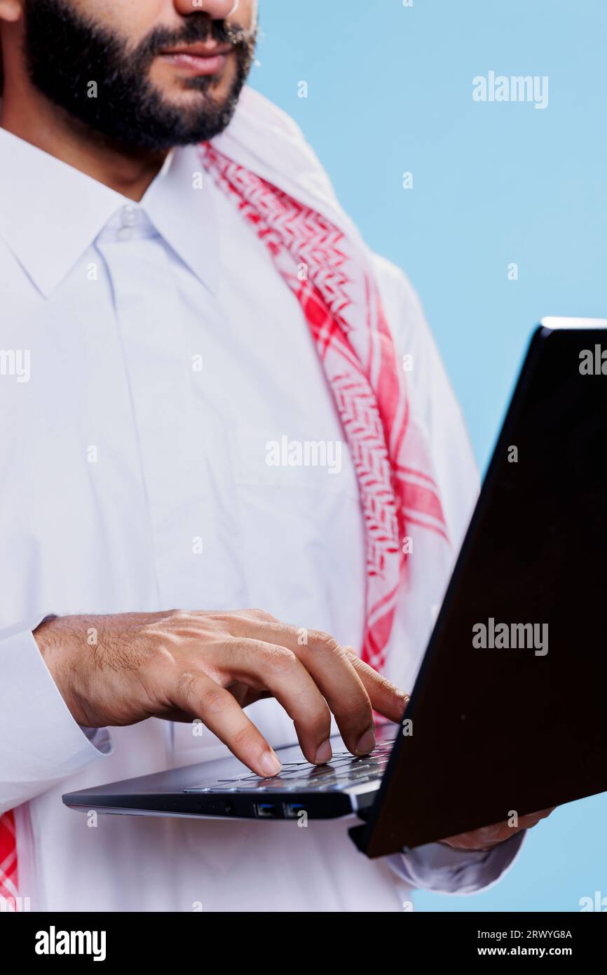 Man wearing traditional muslim clothes typing on laptop keyboard ...