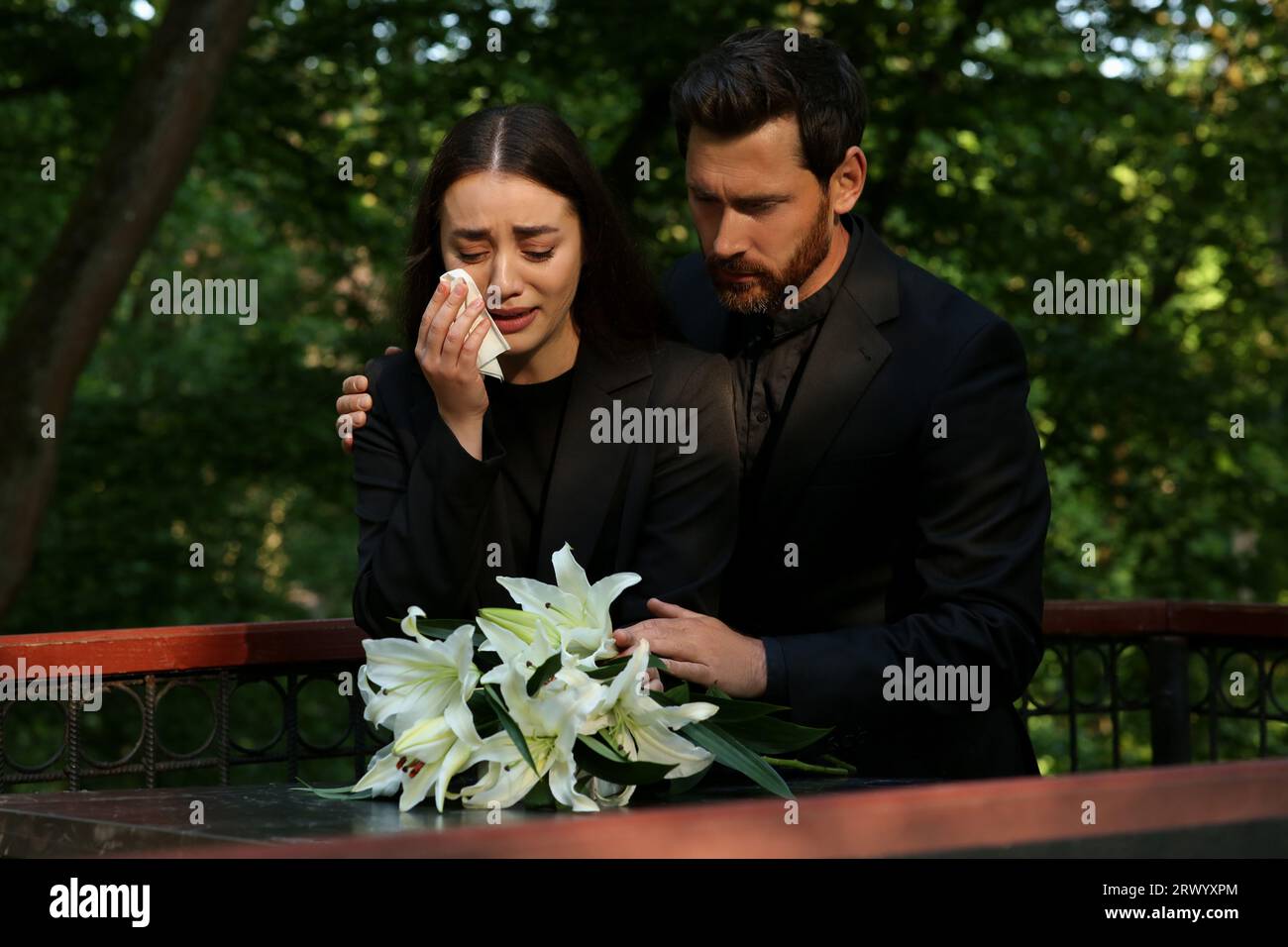 Sad couple mourning near granite tombstone with white lilies at ...