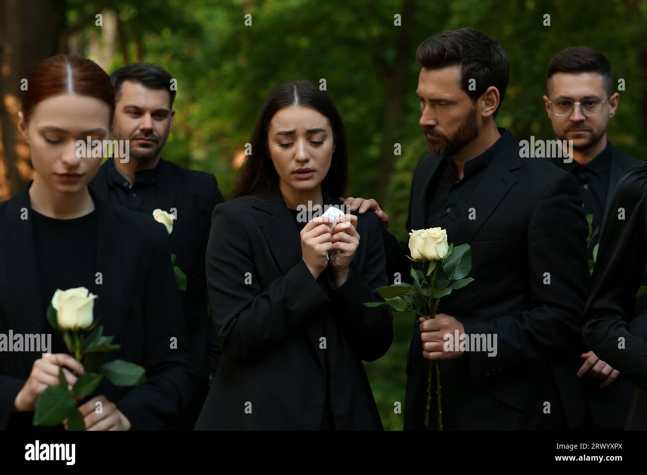 Funeral ceremony. Sad people with white rose flowers mourning outdoors ...