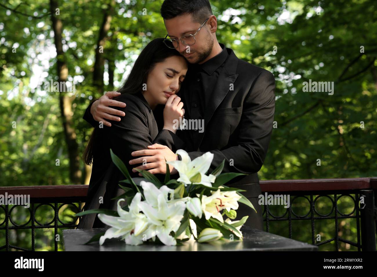 Sad couple mourning near granite tombstone with white lilies at ...