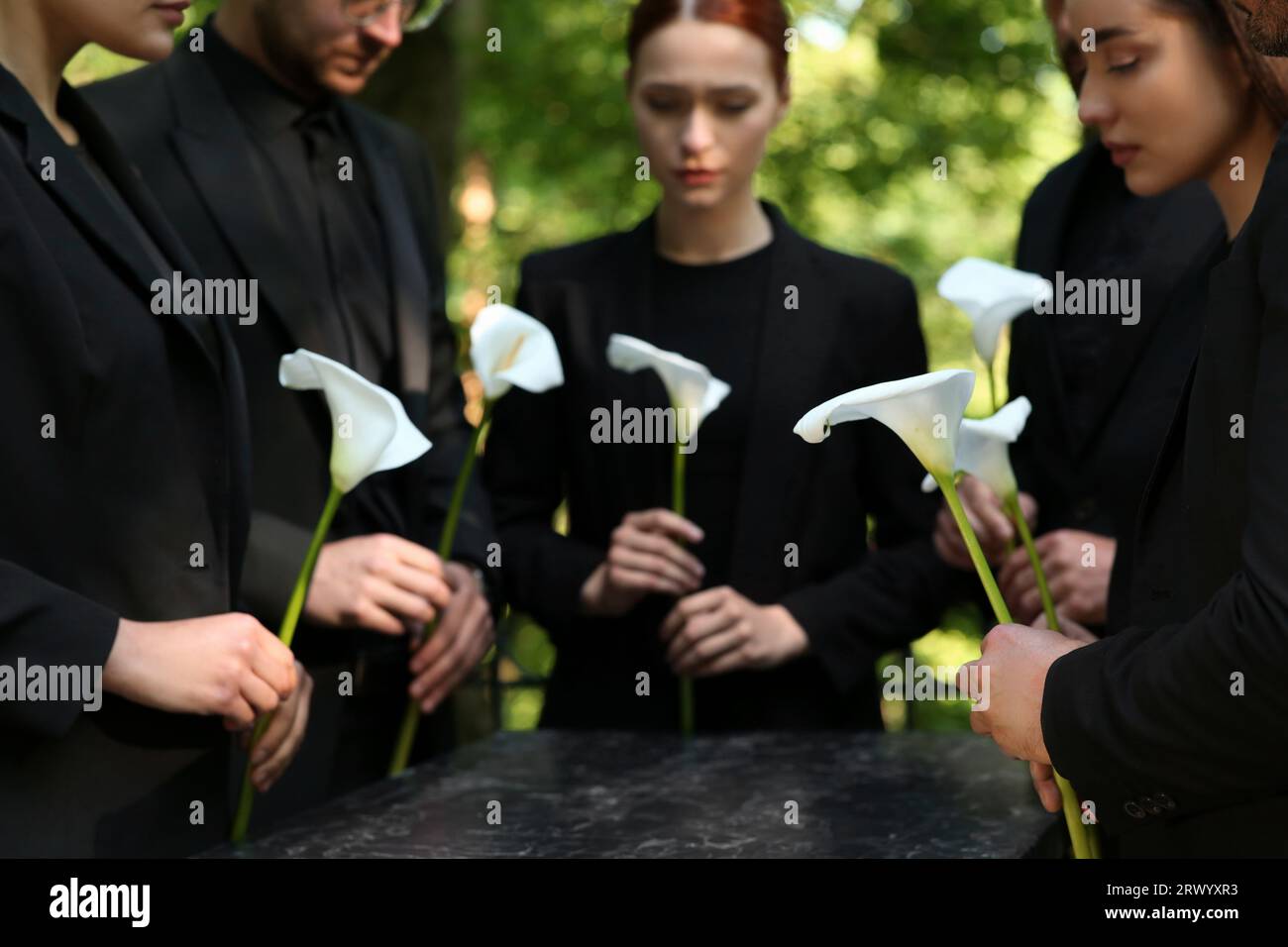 People with calla lily flowers near granite tombstone at cemetery ...
