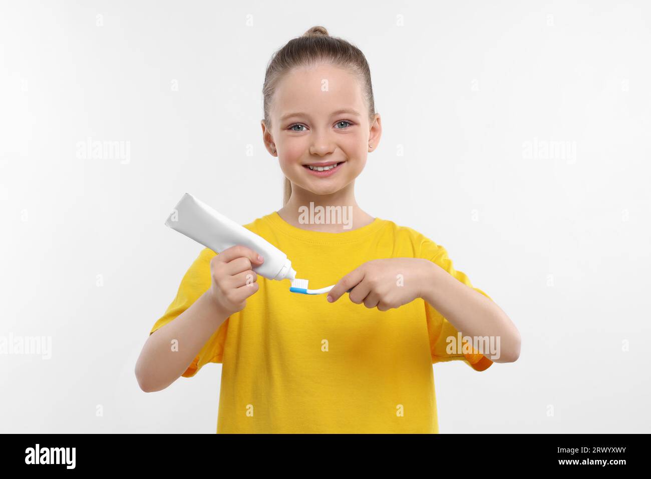 Happy girl squeezing toothpaste from tube onto toothbrush on white ...