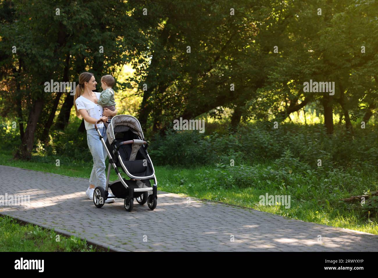 Happy nanny with cute little boy and stroller walking in park, space ...