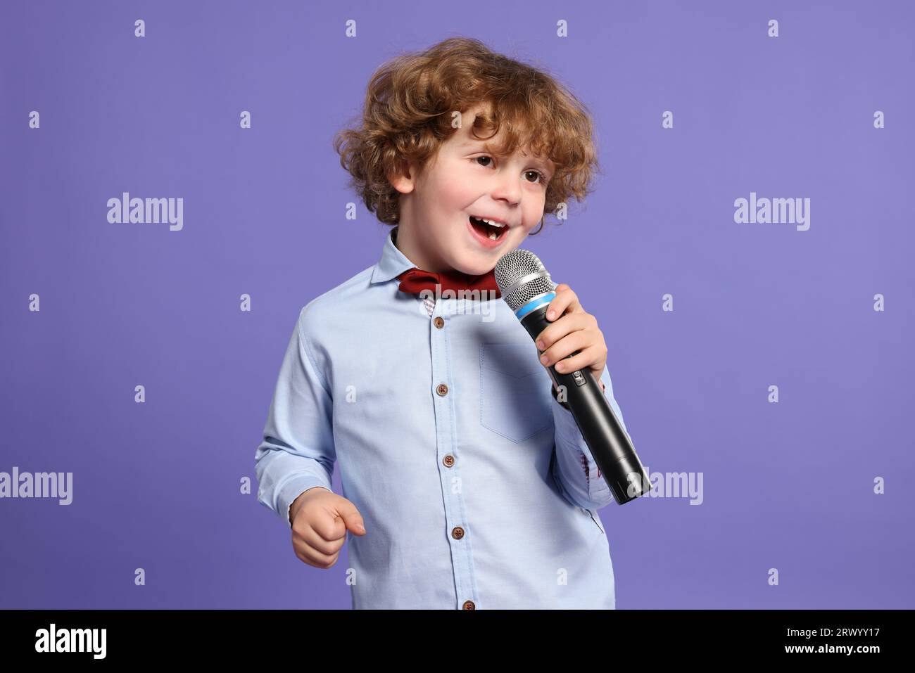 Cute little boy with microphone singing on violet background Stock ...