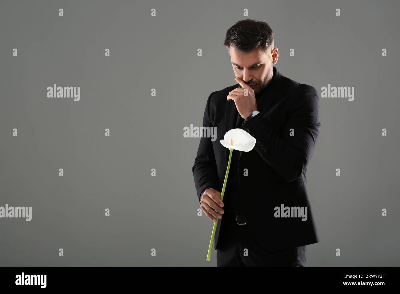 Sad man with calla lily flower mourning on grey background, space for ...