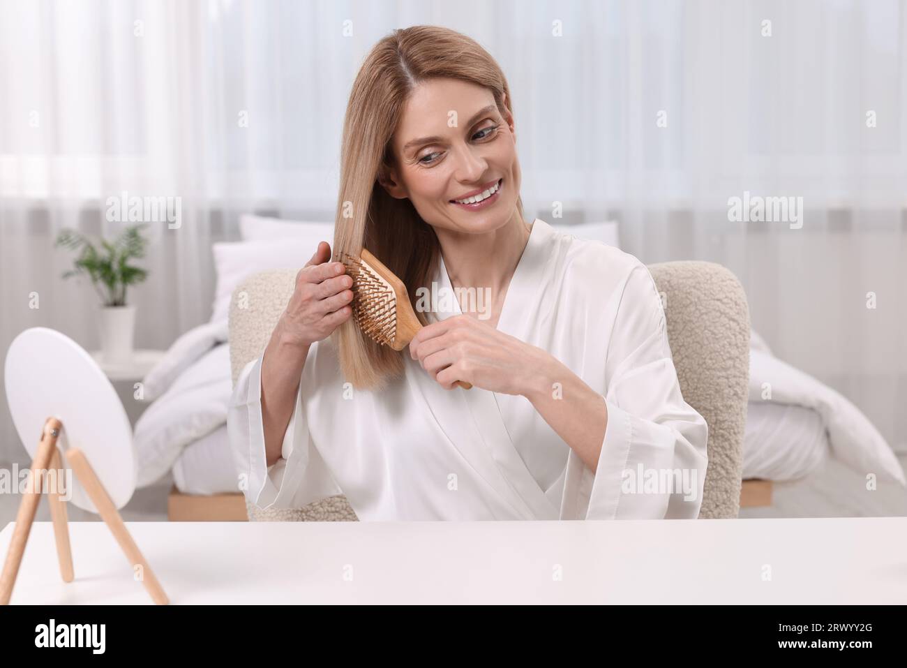Beautiful woman brushing her hair at vanity in bedroom Stock Photo - Alamy