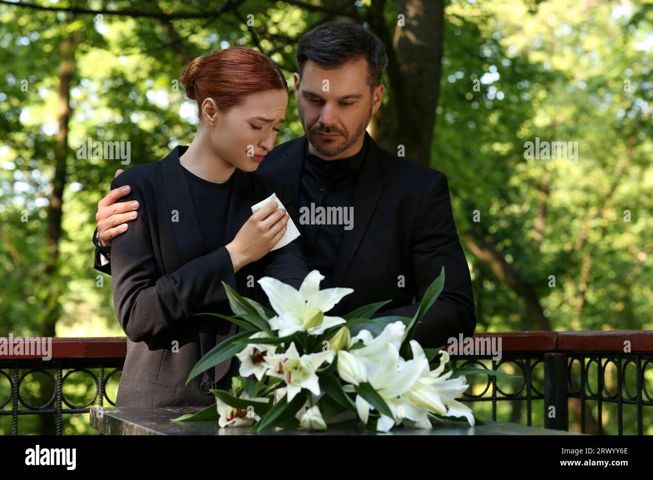 Sad couple mourning near granite tombstone with white lilies at ...
