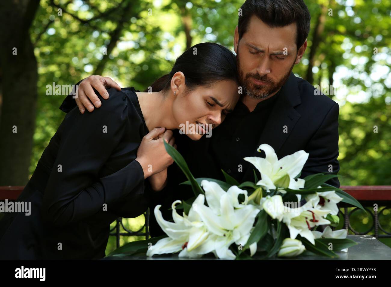 Sad couple mourning near granite tombstone with white lilies at ...