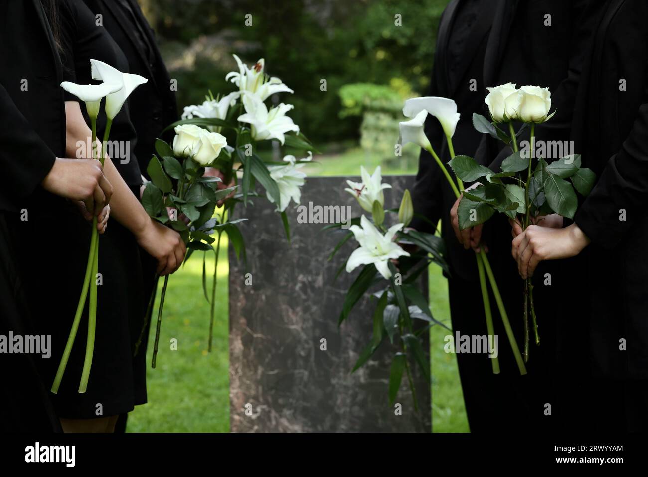 People with flowers near granite tombstone at cemetery outdoors ...