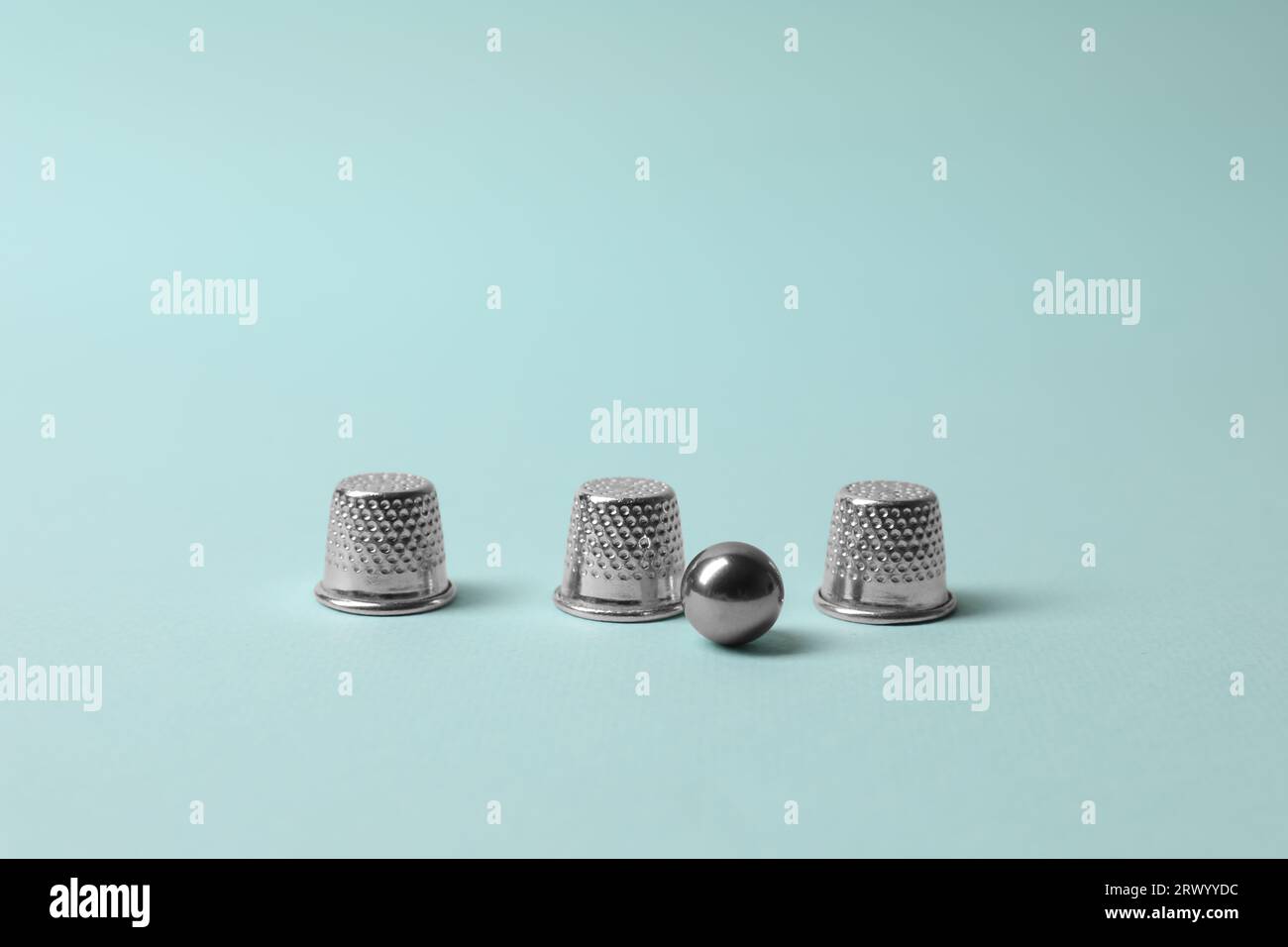 Metal thimbles and ball on light blue background. Thimblerig game Stock ...