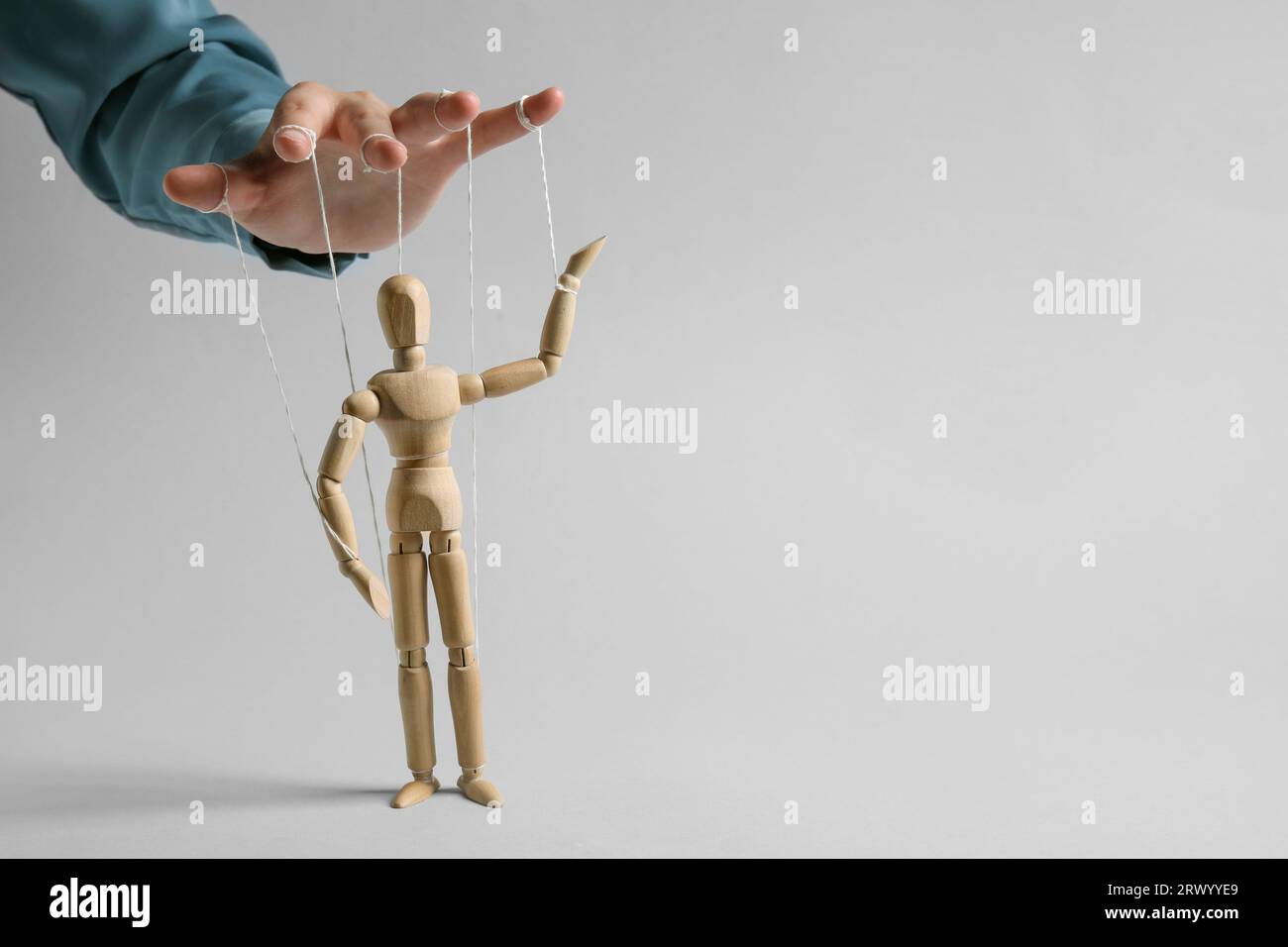 Woman pulling strings of puppet on light grey background, closeup ...
