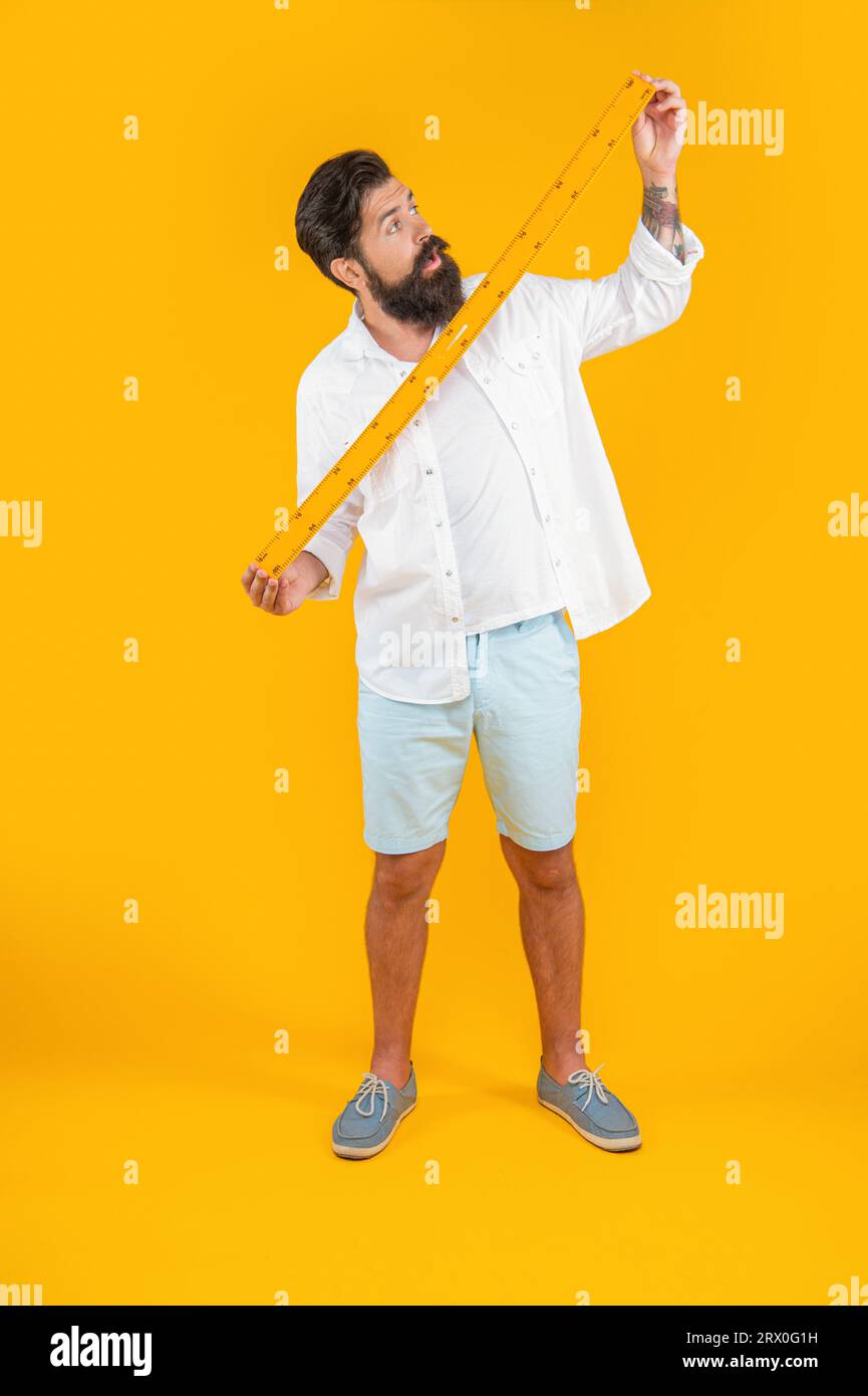photo of surprised man hold school ruler isolated on yellow background ...