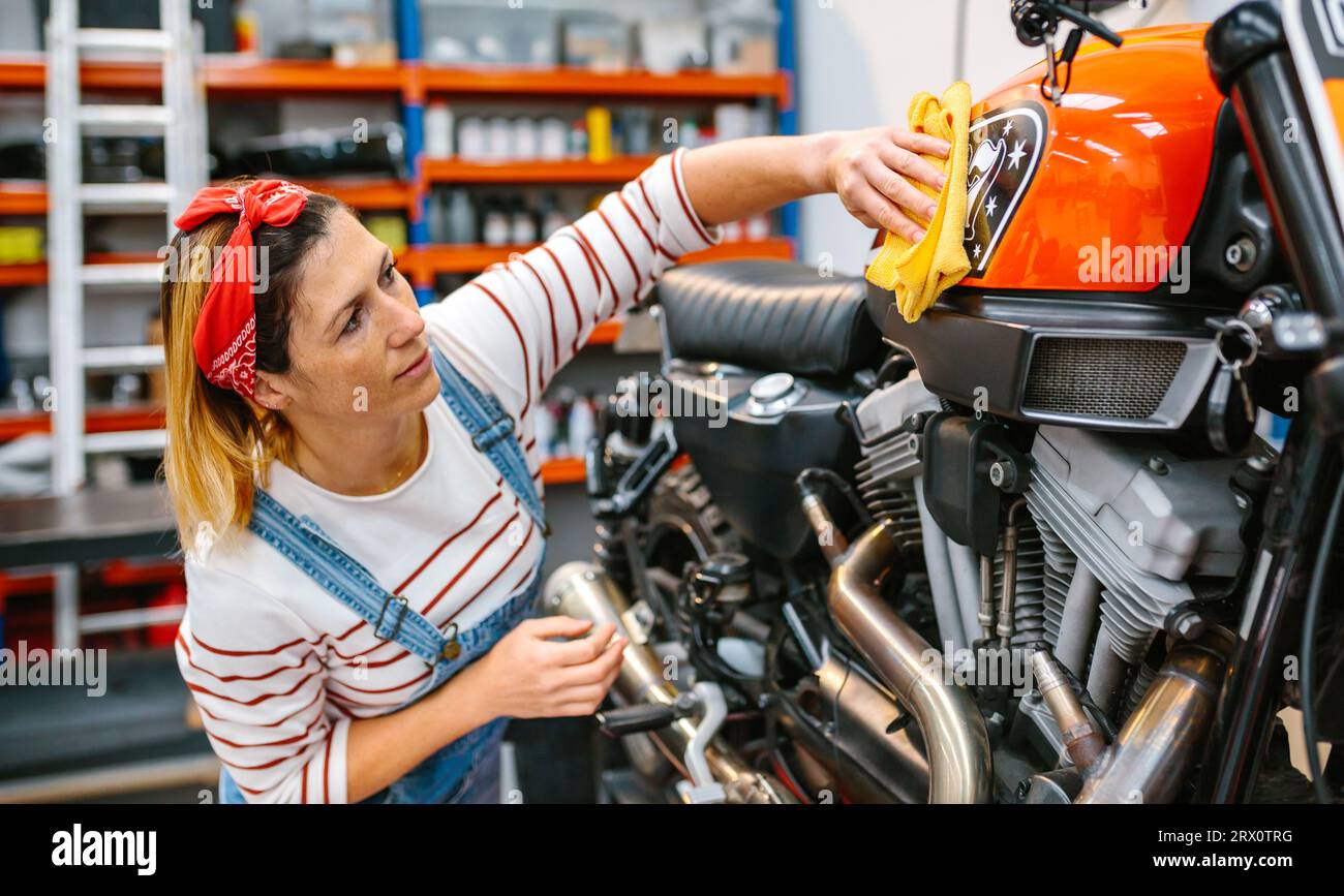 Mechanic woman cleaning motorcycle with cloth and polish on factory ...