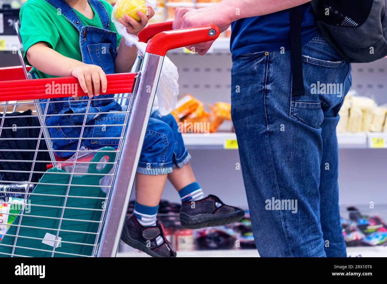 Boy sits in the basket trolley on wheels in store. A man with a child ...