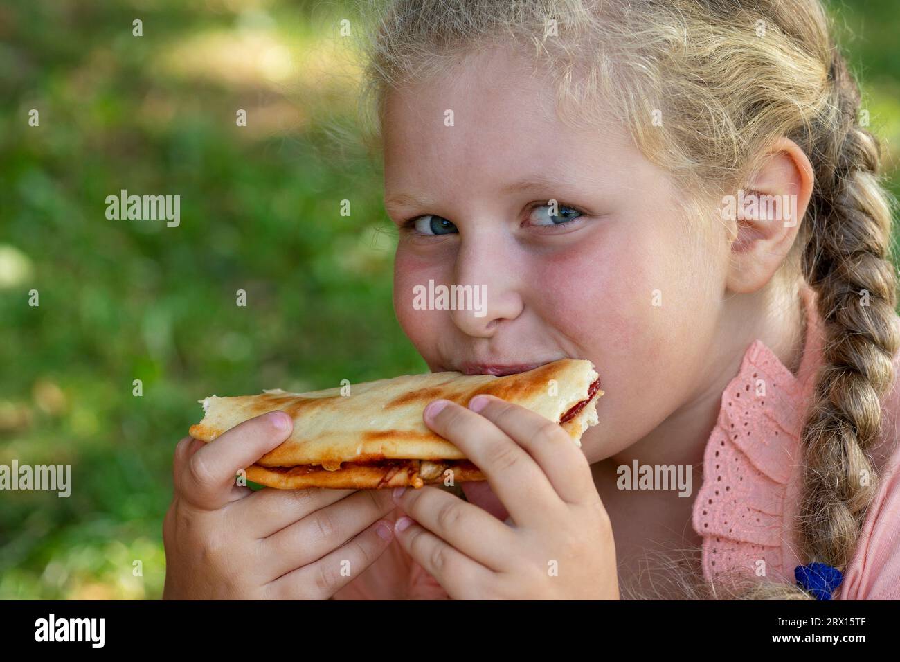 Cheerful girl eats a pie. Happy child holding a piece of pizza in his ...