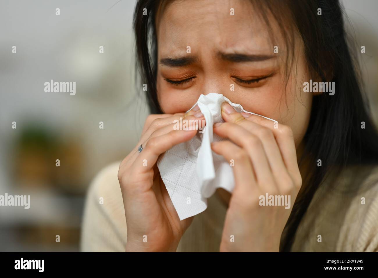 Sick woman having allergy symptoms ,blowing nose and sneezing in tissue ...