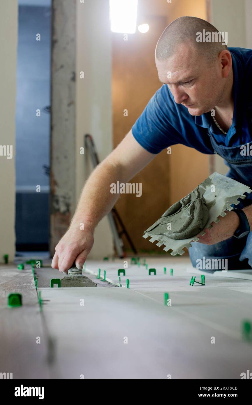 Tiler placing ceramic wall tile in position over adhesive with lash ...