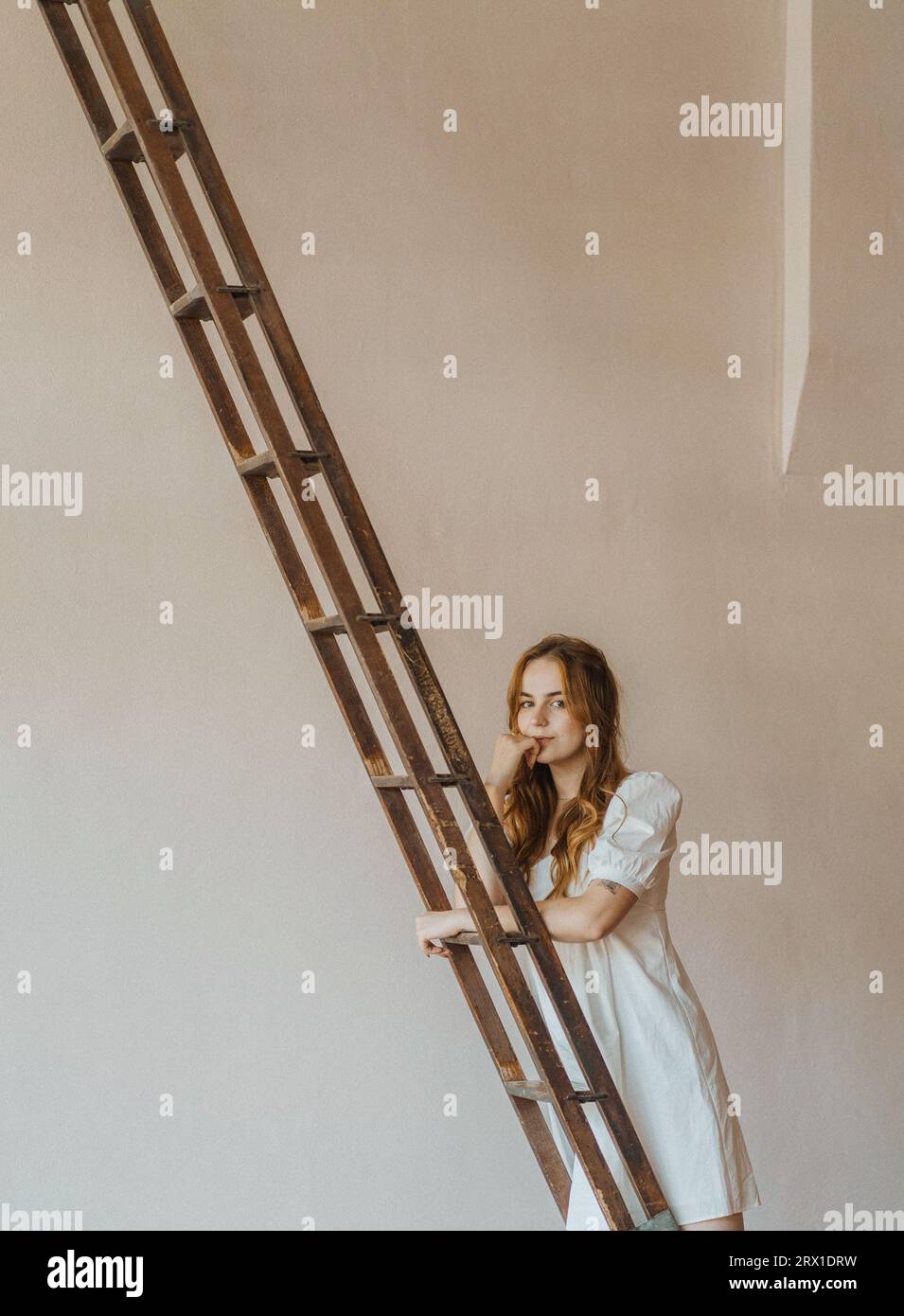Red-haired model in white poplin dress leans on a vintage ladder Stock ...