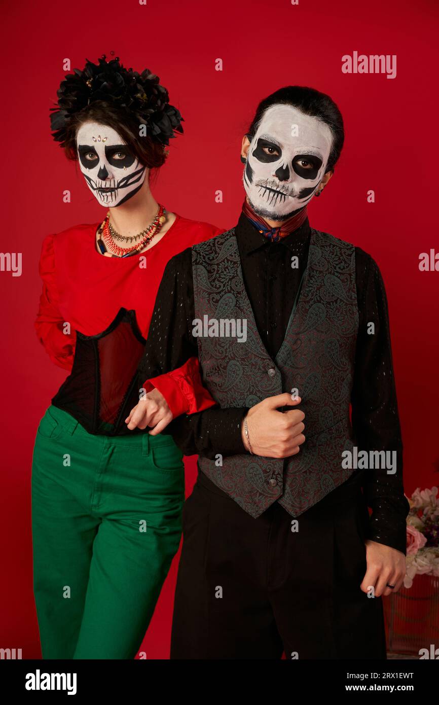 young couple in scary skeleton makeup and stylish clothes posing on red ...