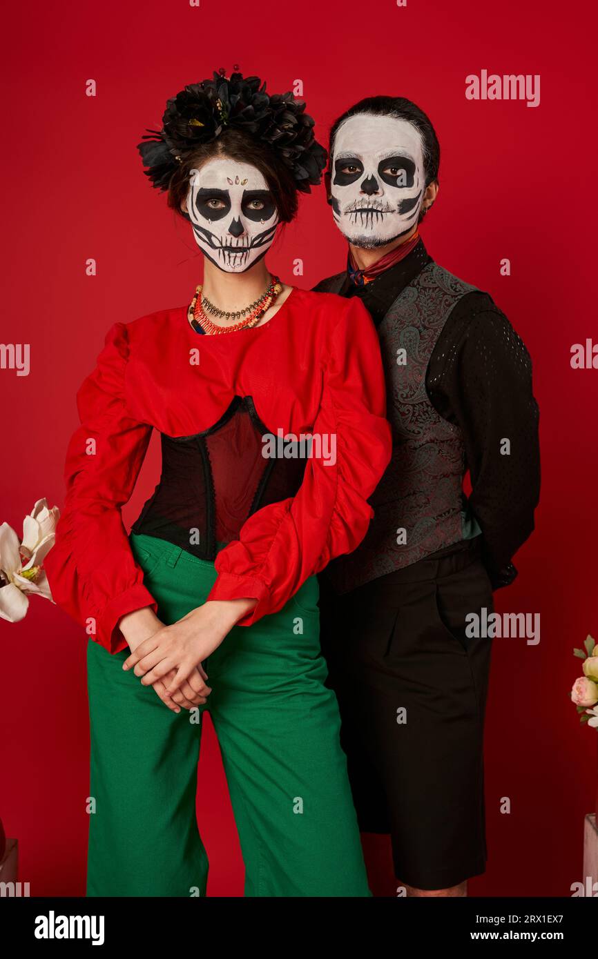 couple in festive attire and catrina makeup posing on red backdrop, dia ...