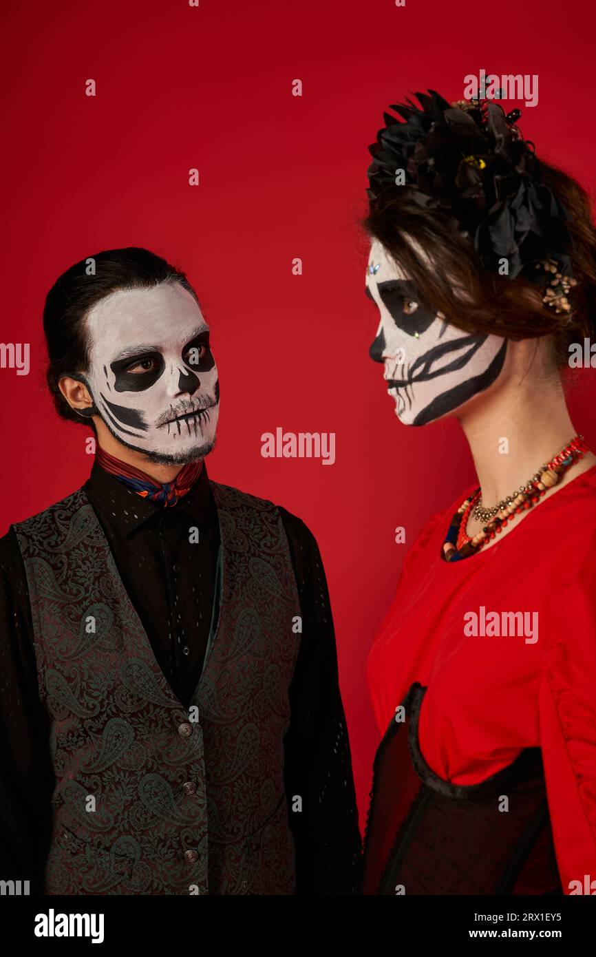 spooky man in sugar skull makeup looking at woman in black wreath, dia ...