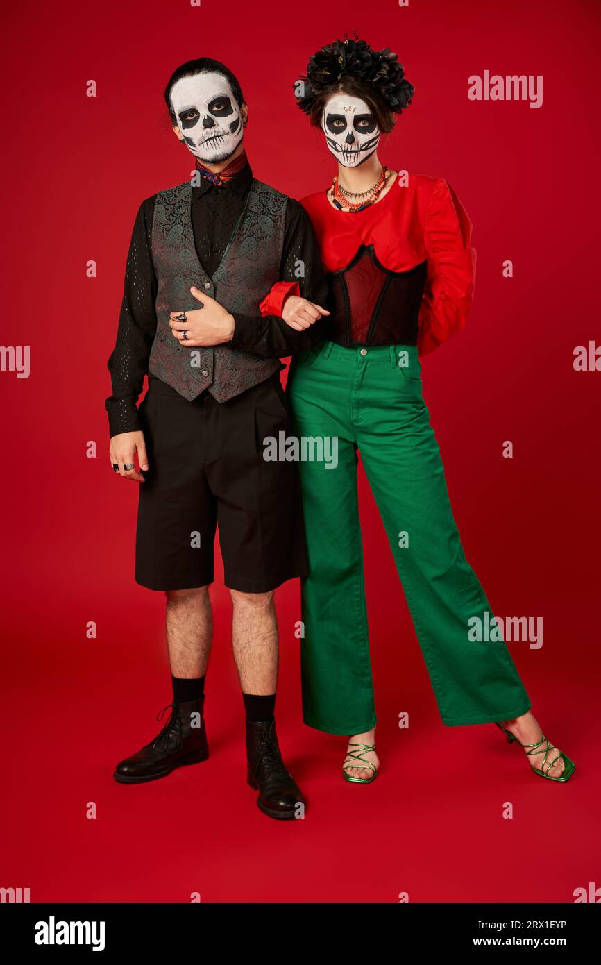 full length of couple in trendy clothes and skeleton makeup on red, dia ...