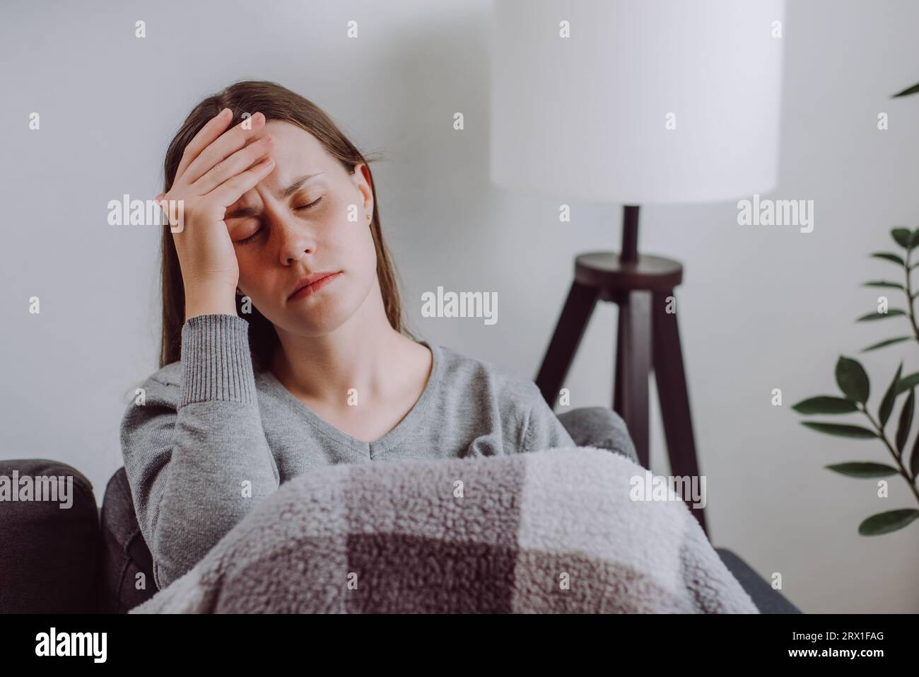 Sick unhappy brunette young woman covered in blanket sitting on couch ...