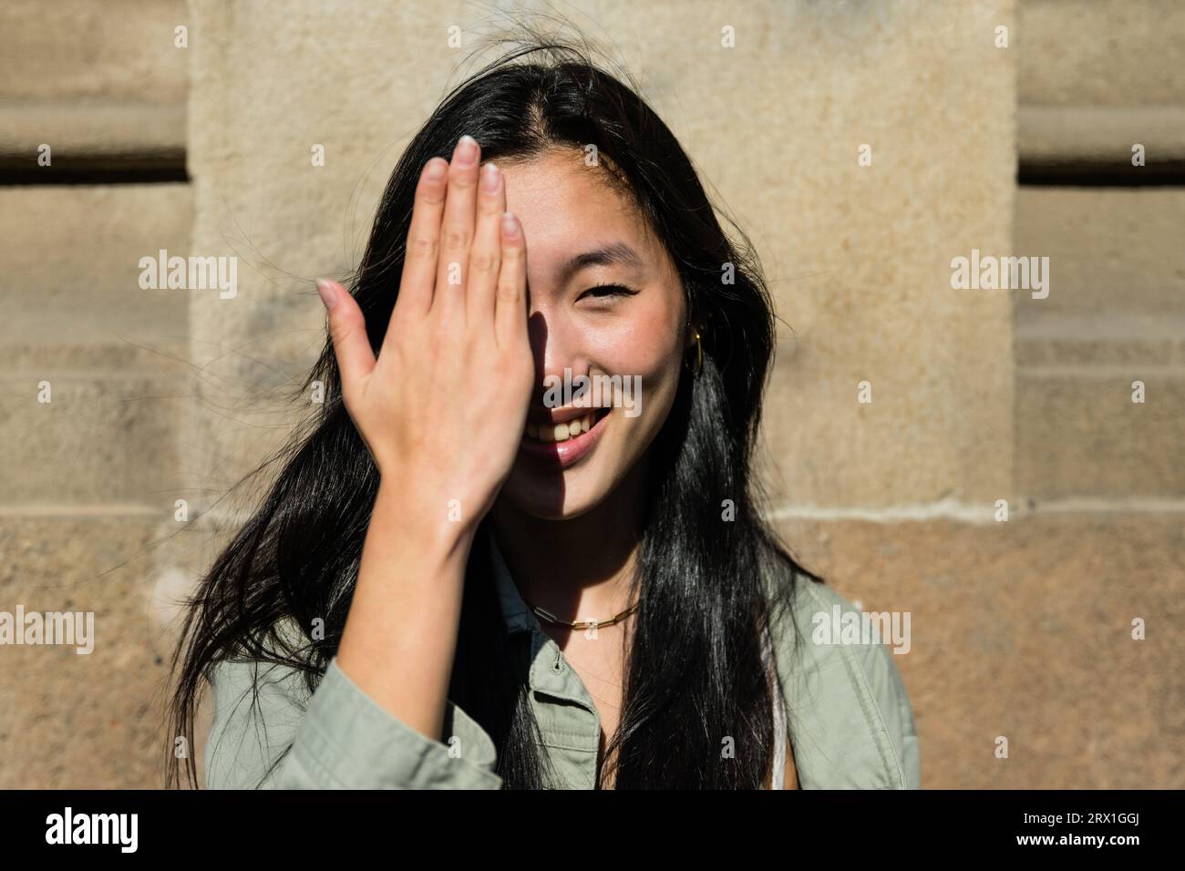 Happy young woman covering one eye with her hand outside Stock Photo ...