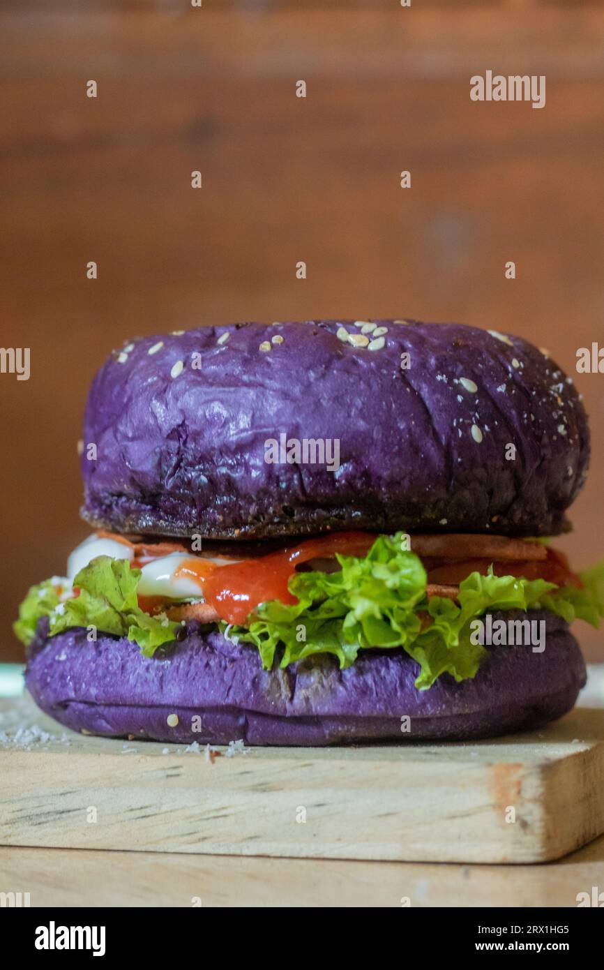 close up photo of a home-made purple burger placed on a ceramic table ...