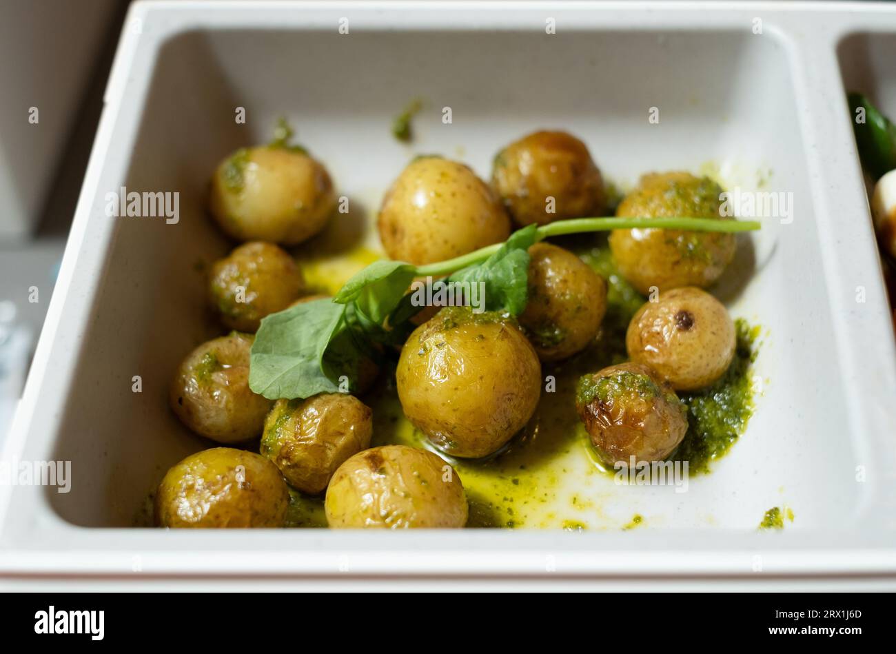 Photograph of roasted new potatoes with pesto and a herb draped across ...