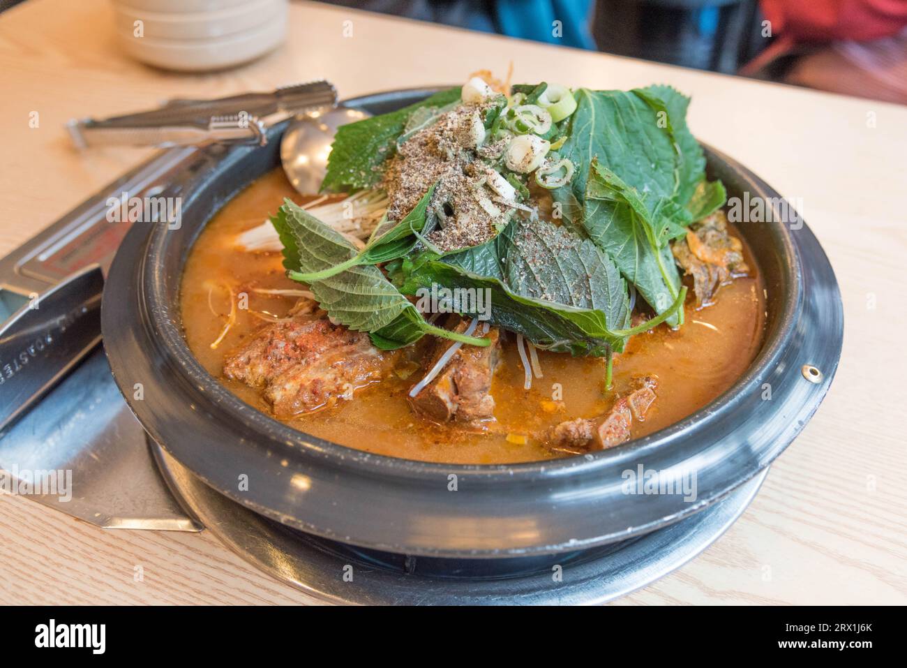 Gamjatang, a Korean pork bone soup in a pot, topped with perilla leaves and perilla powder Stock ...